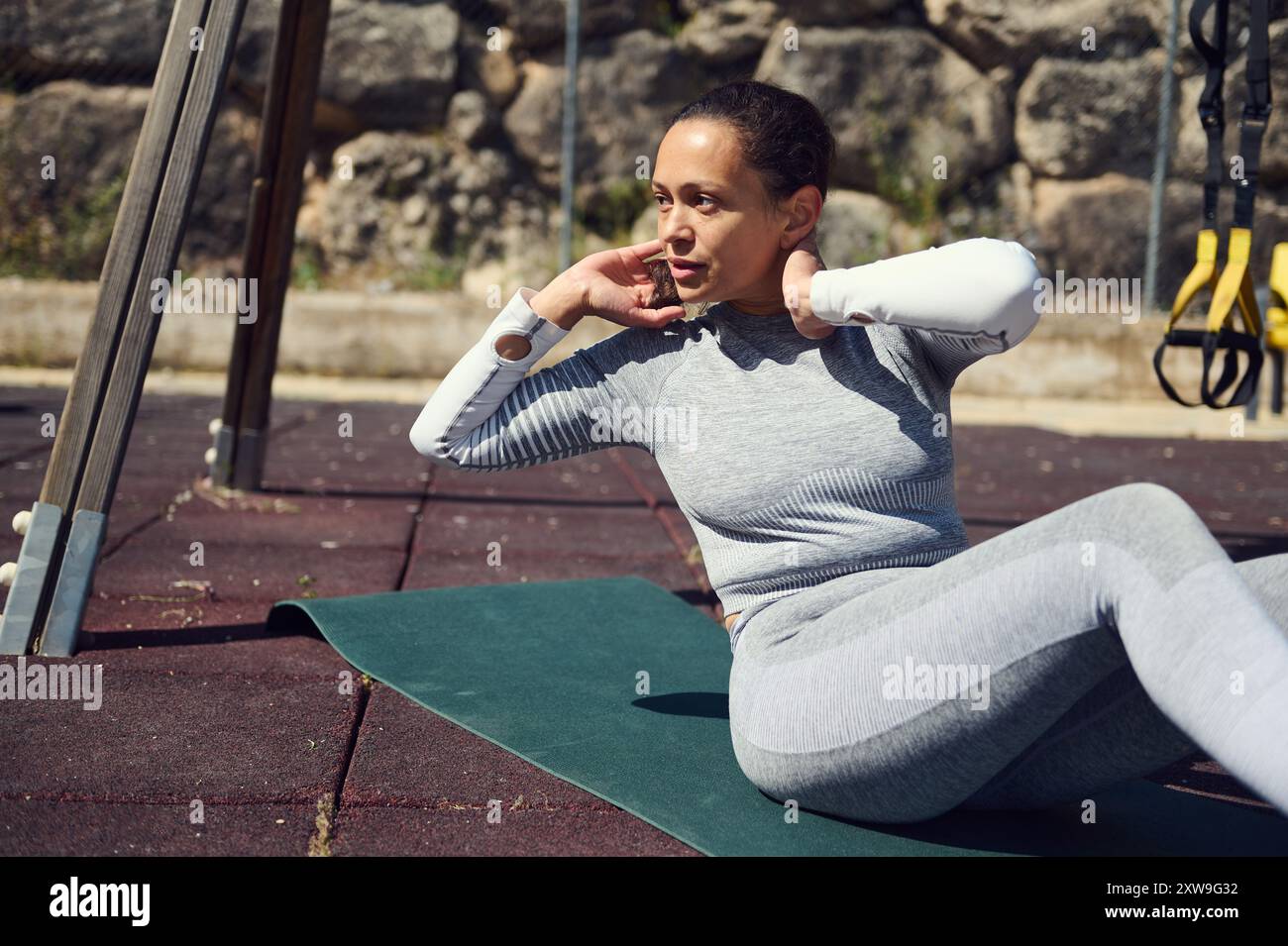Woman doing sit-ups on a mat outdoors, showing strength and fitness in ...