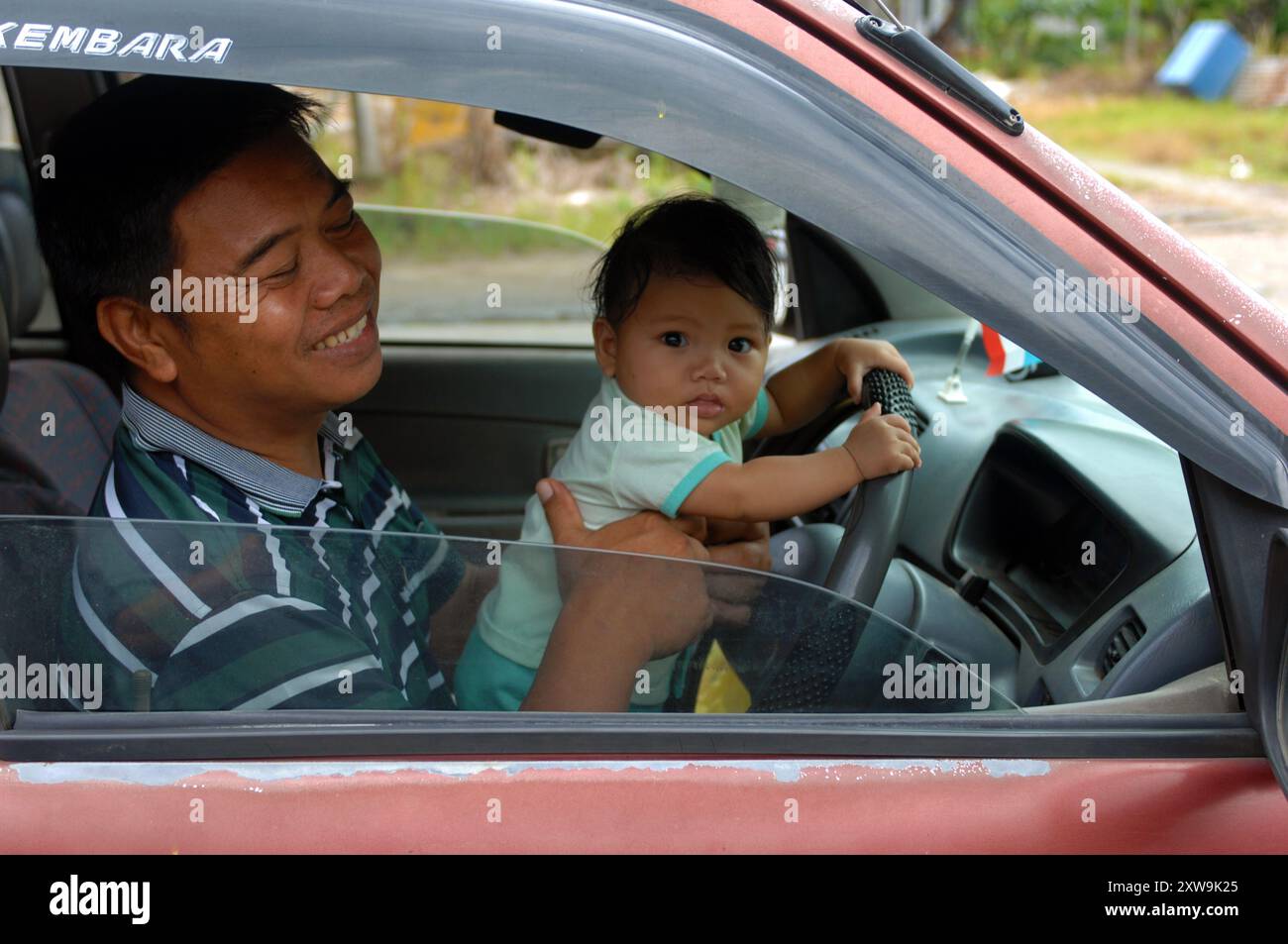 Father allowing son to hold the driving wheel of a car, Bongkud, Ranau, Sabah, Malaysia Stock ...