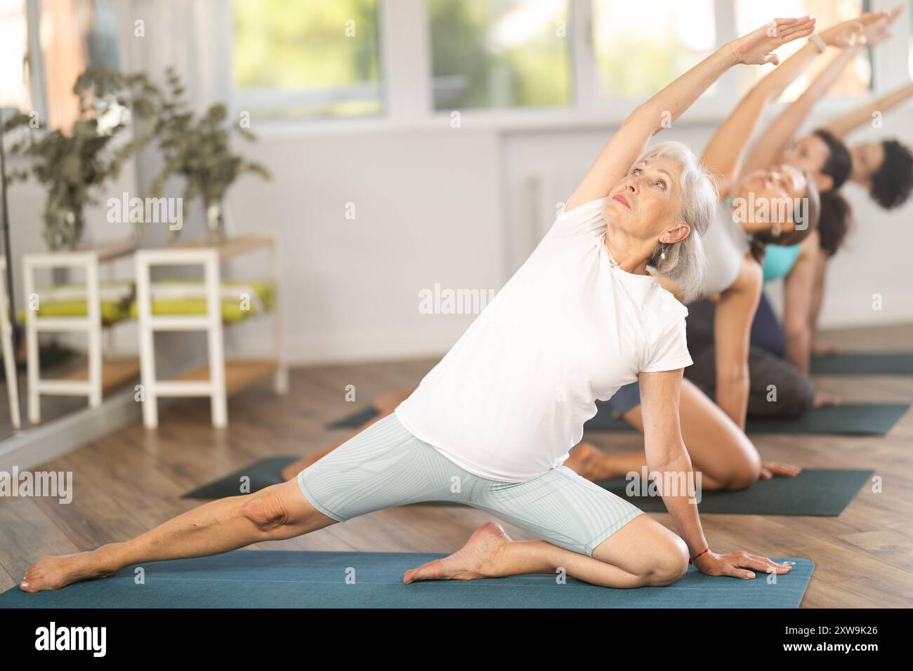 Senior woman performing Gate Pose during group yoga practice Stock ...