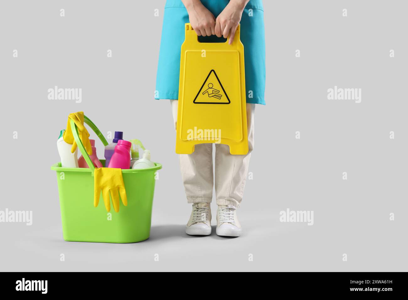 Female janitor with caution sign and cleaning supplies on light ...
