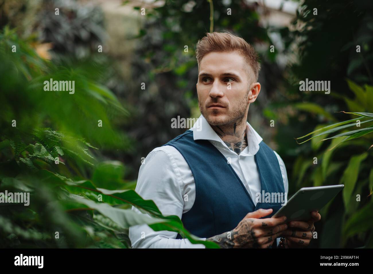 Handsome businessman with tablet, standing in botanical garden, in the ...