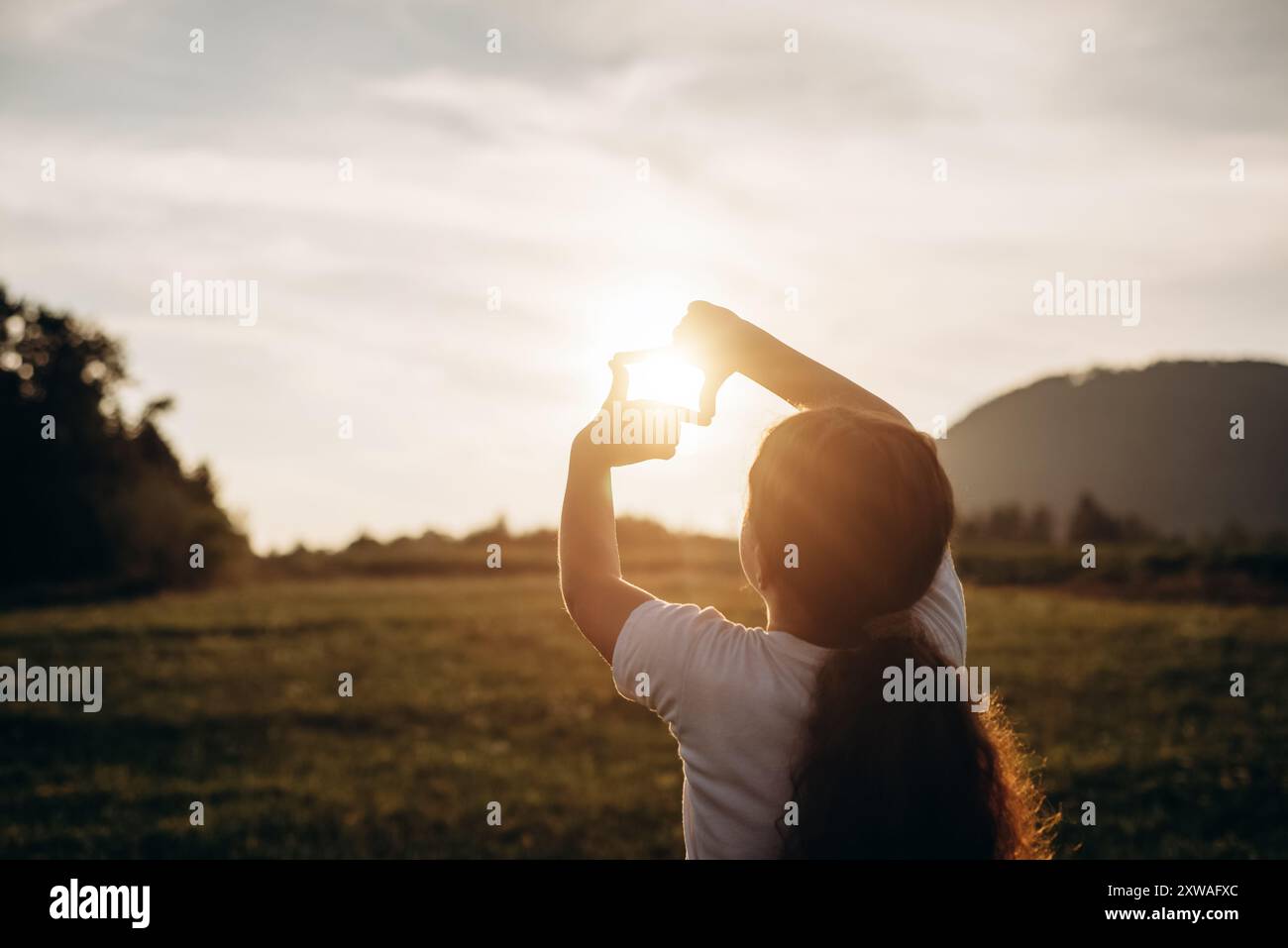 Preteen girl making frame gesture at amazing sunset in beautiful summer ...