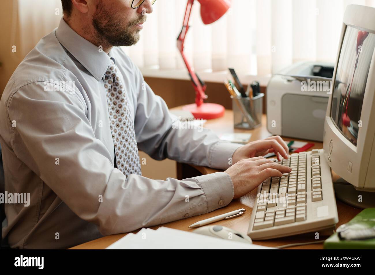 Man sitting at desk, using computer while writing, wearing glasses and ...