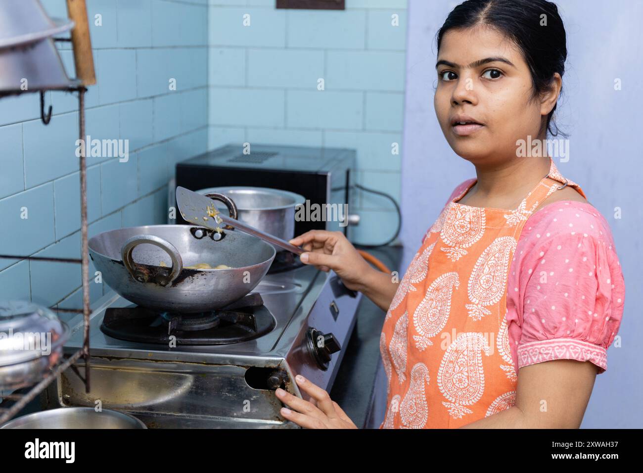 An Indian housewife wearing cooking apron in kitchen making food in ...