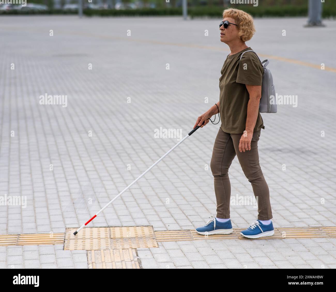 An elderly blind woman walks with a cane along a tactile tile Stock ...