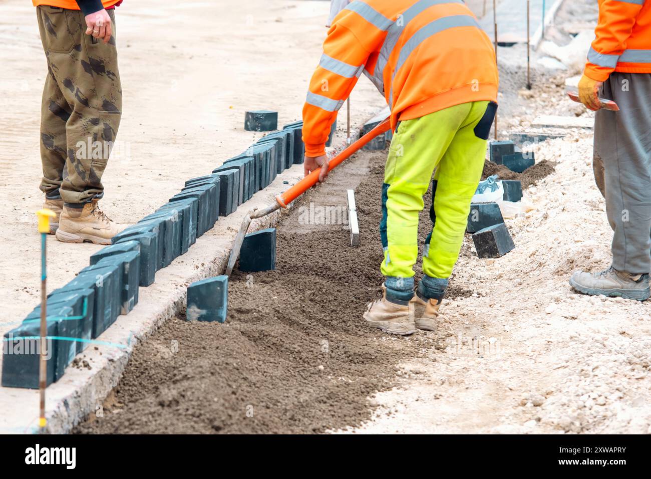 Groundworker in orange hi-viz levelling semi-dry concrete and laying ...