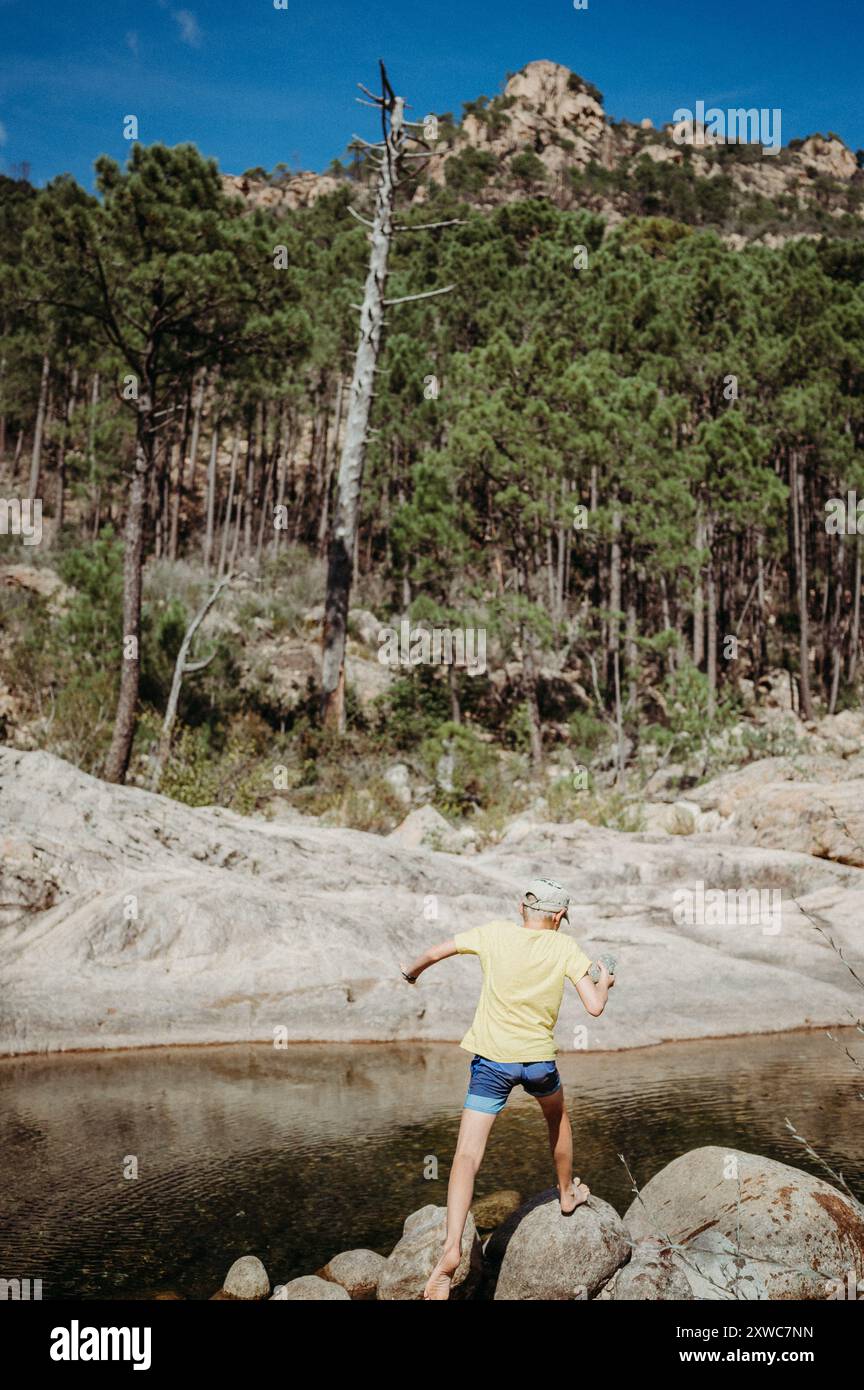 Boy jumping on rocks in a Corsican river with a forest backdrop Stock ...
