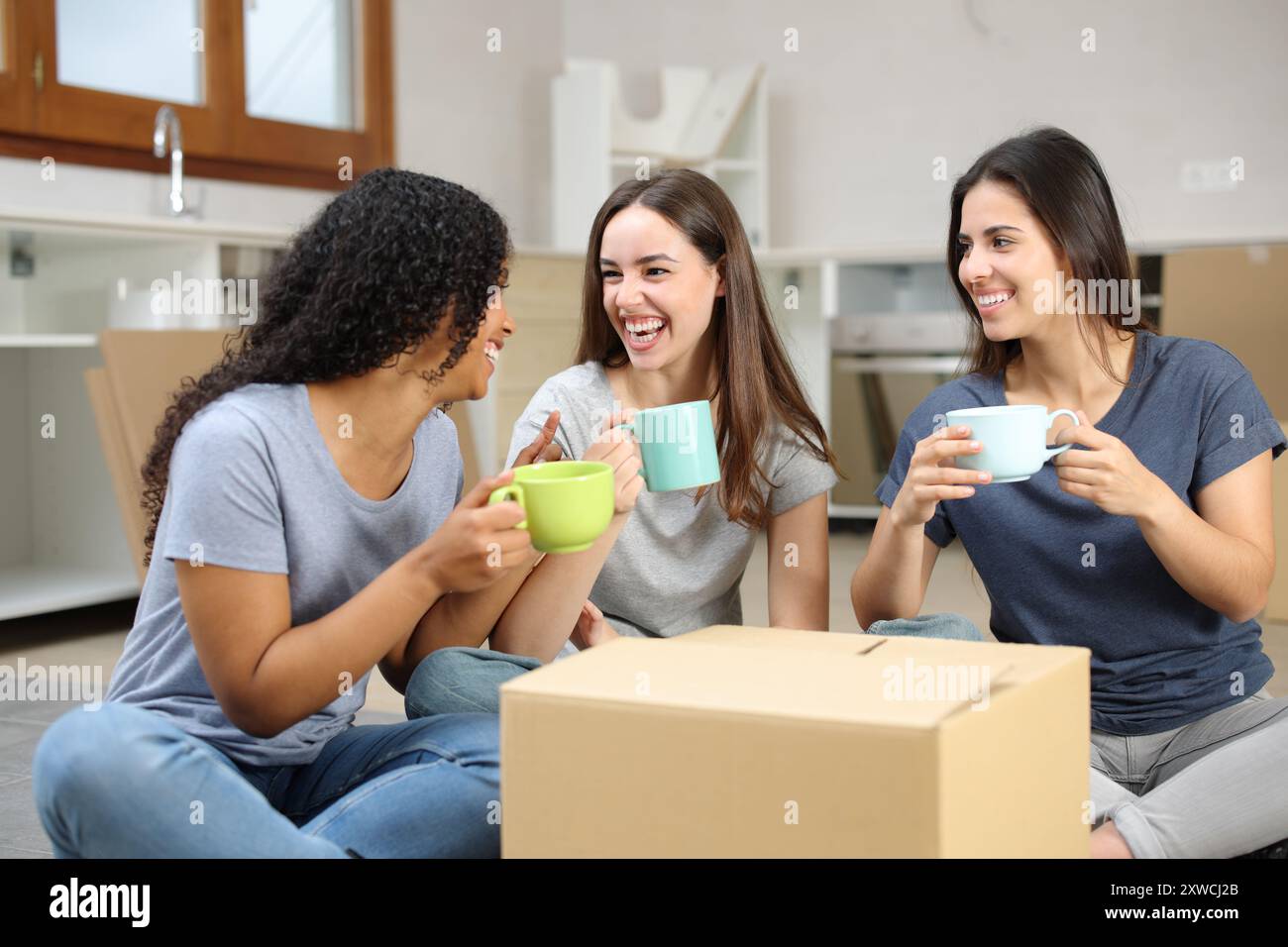 Three happy roommates talking and resting moving home in the kitchen ...