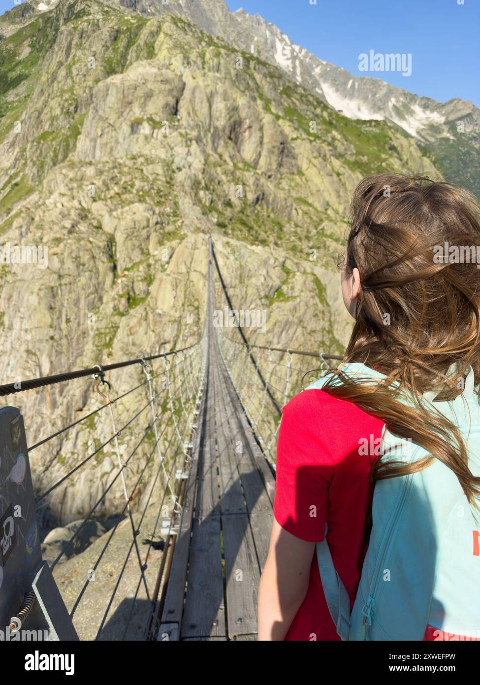Young woman crossing the chasm on the rope bridge with the backpack ...