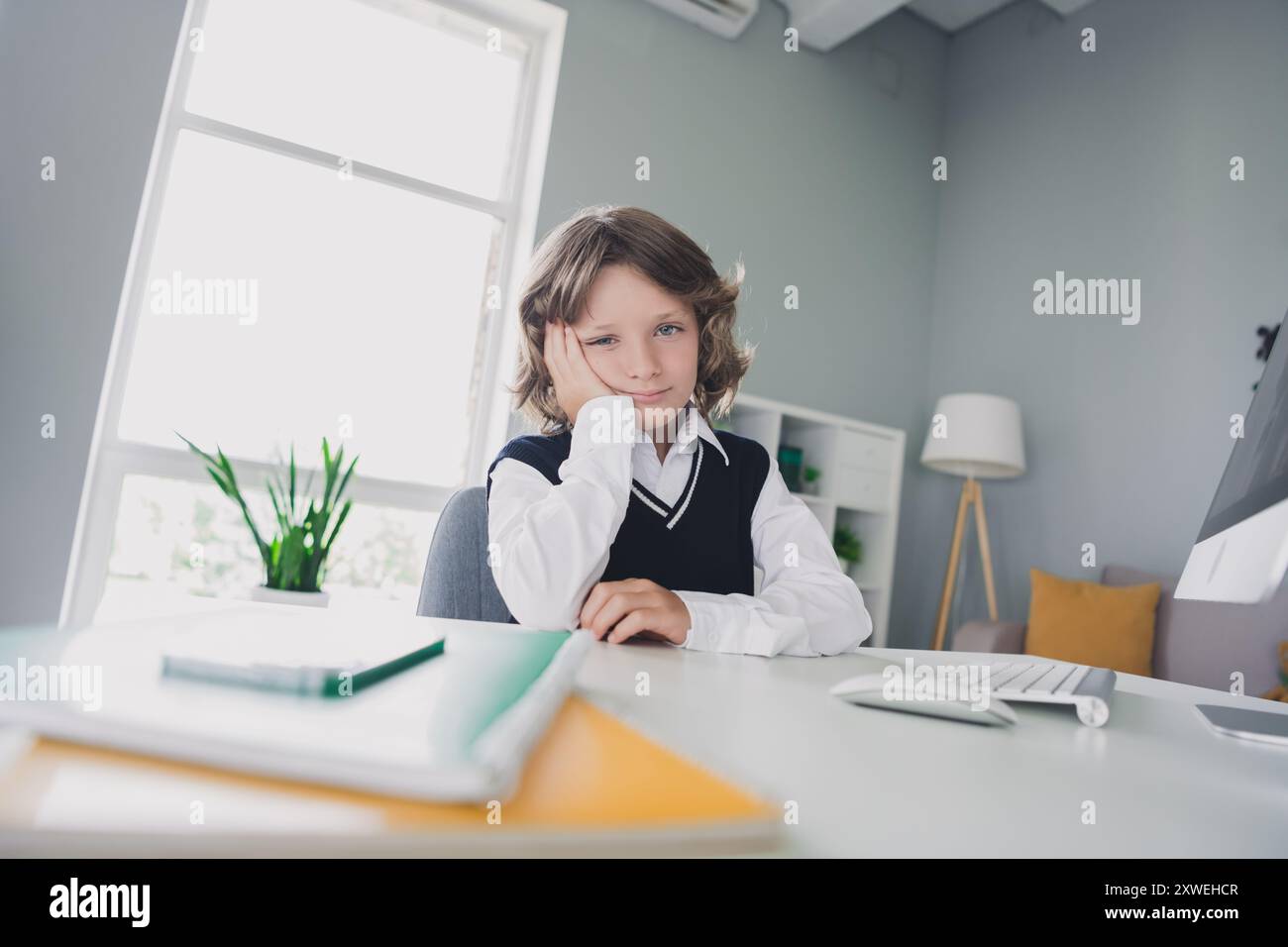 Portrait of tired adorable learner boy sitting chair desktop listen ...