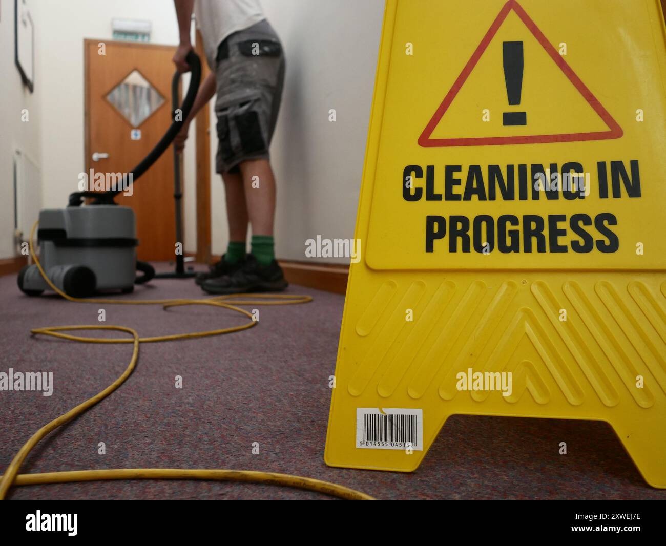 Cleaner at work vacuuming office corridor using a cleaning in progress ...