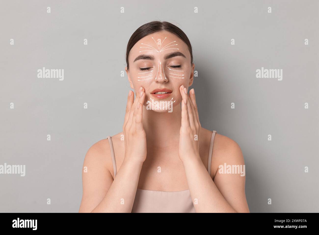 Beautiful young woman doing face massage with fingers on grey ...
