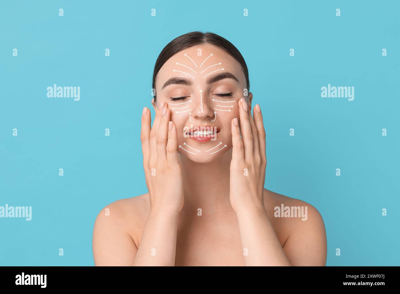 Beautiful young woman doing face massage with fingers on light blue ...