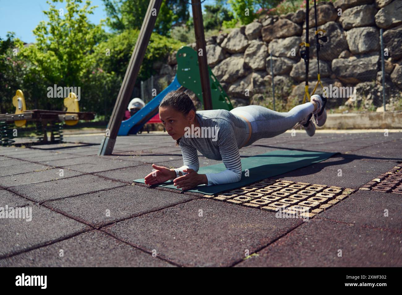 A woman engages in a forearm plank exercise in a playground ...