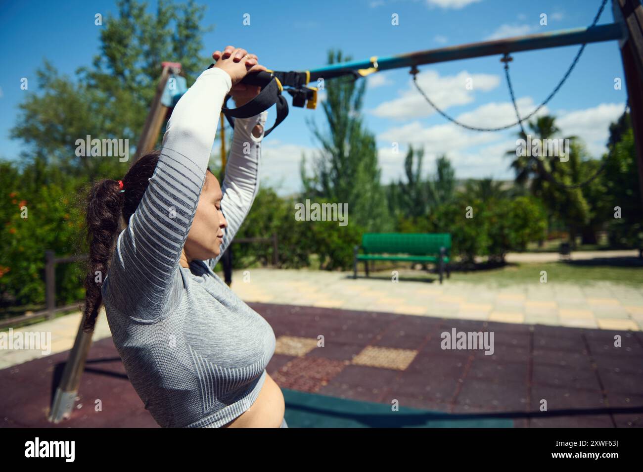 Woman using resistance band in park to enhance fitness routine. Bright ...