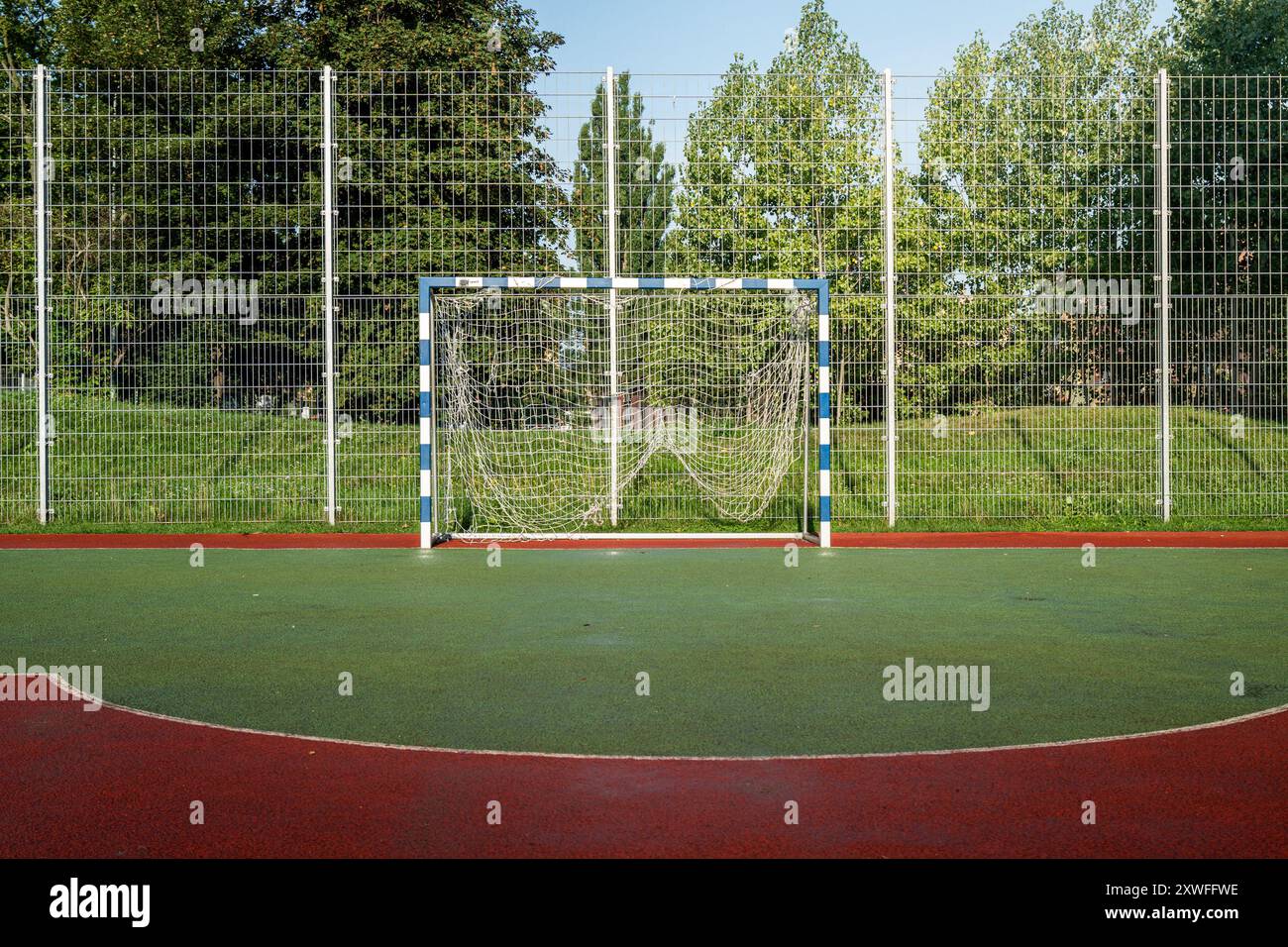A soccer goal stands on a colorful outdoor pitch surrounded by a fence ...