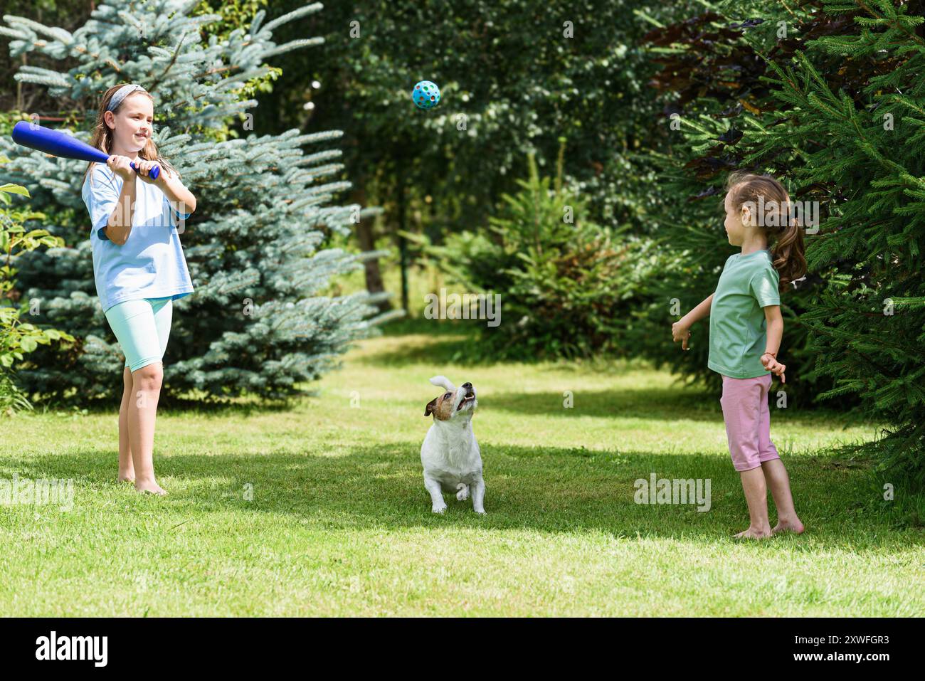Girls playing with baseball bat in garden and dog catching ball Stock ...
