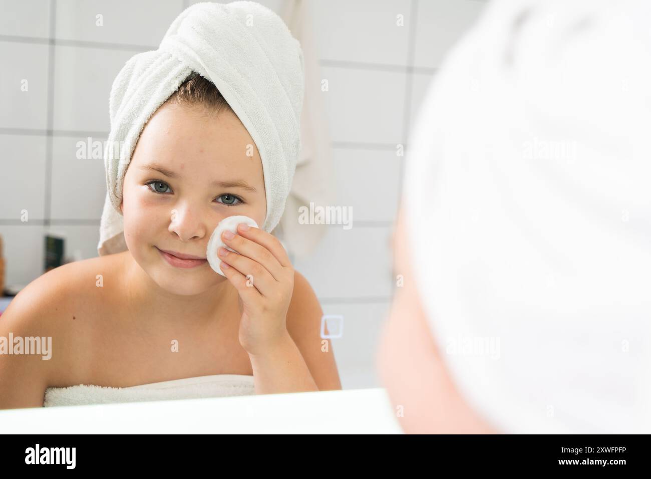 A little teenage girl wipes the skin of her face with a cotton mug with ...