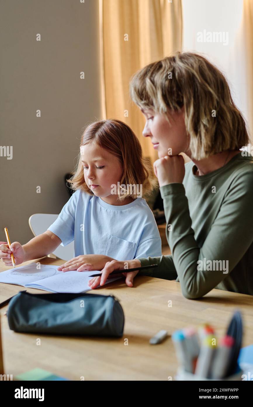 Young blonde mother sitting next to her lovely daughter while they ...
