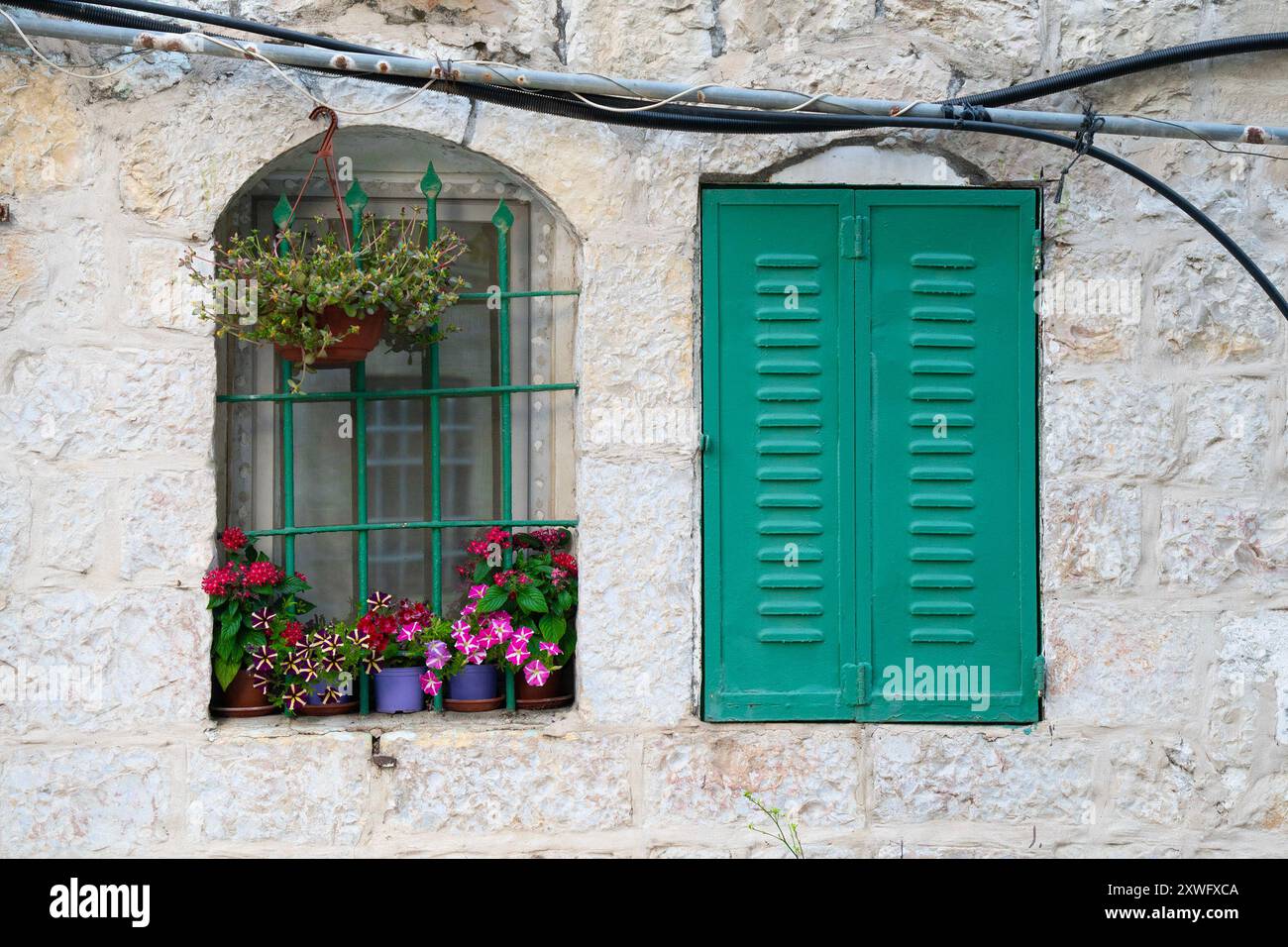 Green metal shutters and flowers in an arched window in a stone wall ...