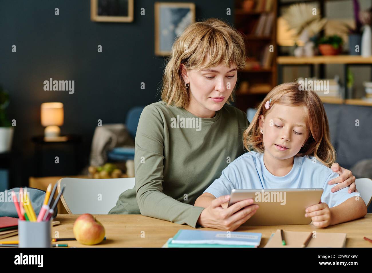 Mom and her daughter with similar haircuts sitting at wooden desk and ...