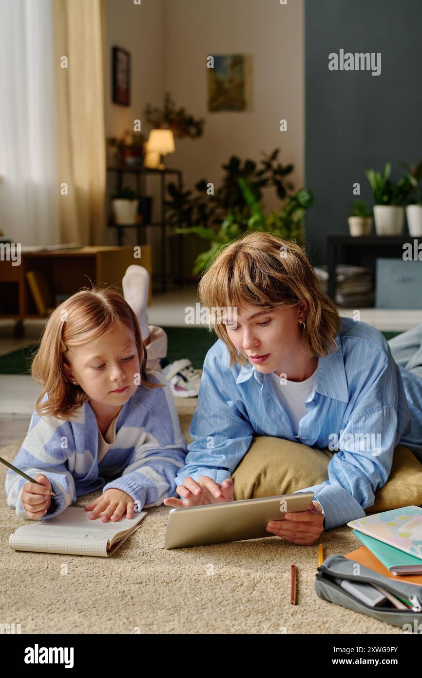 Mom and her kid studying together on floor, mother showing examples via ...