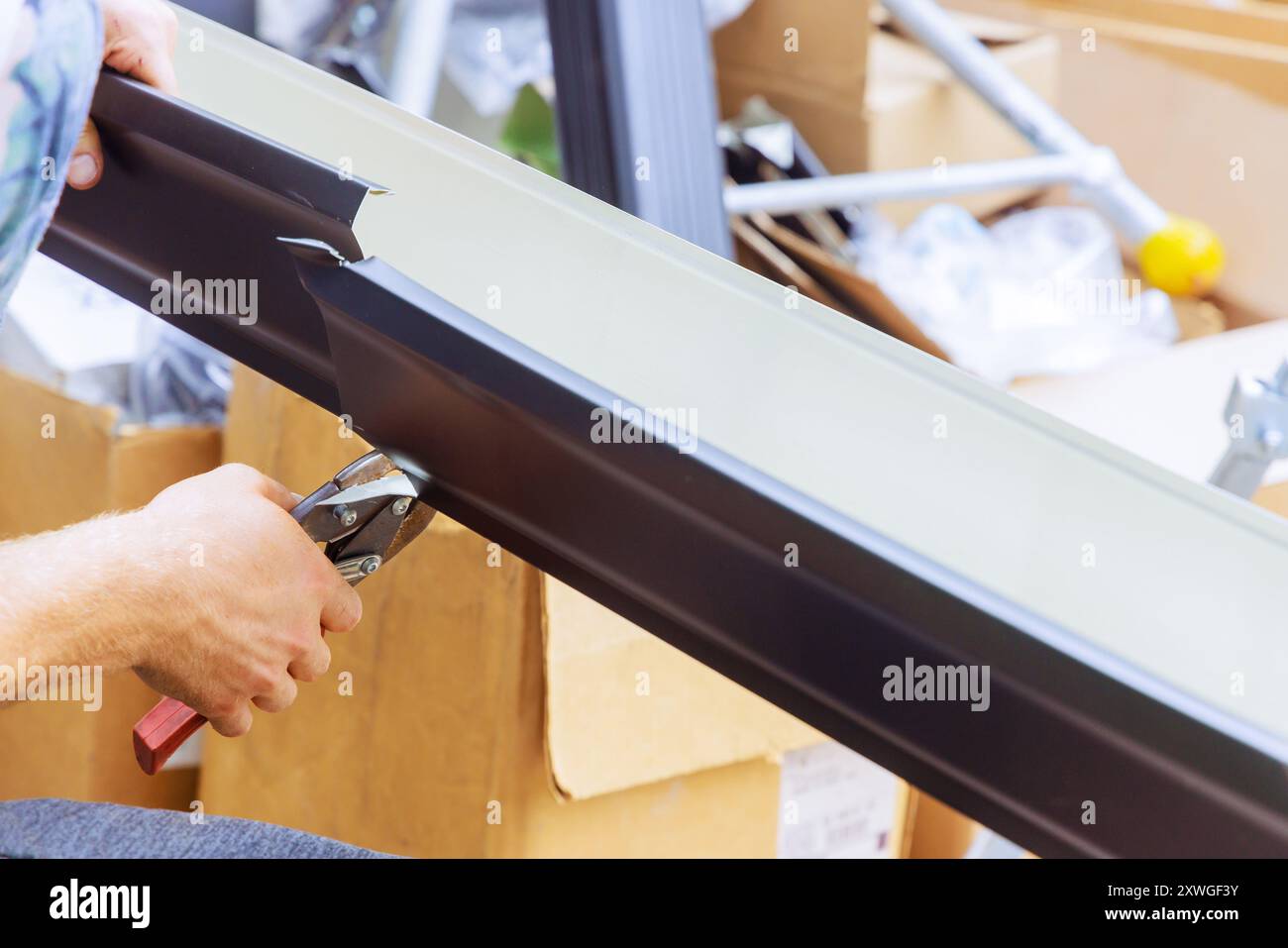After aluminum rain gutters have been bent on machine tool, worker cuts ...