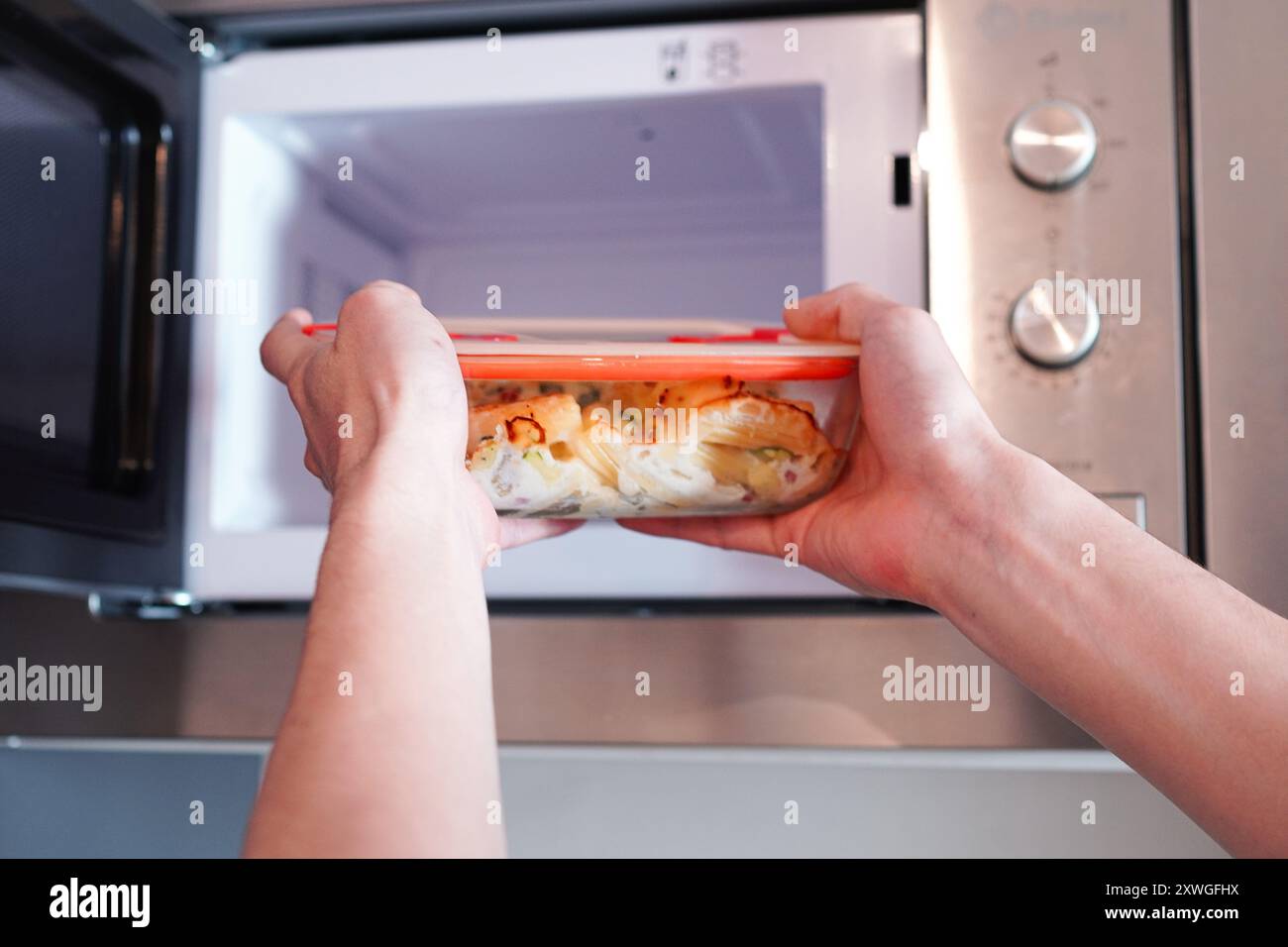 Young Man warms heat-resistant glass Tupperware in microwave oven in ...