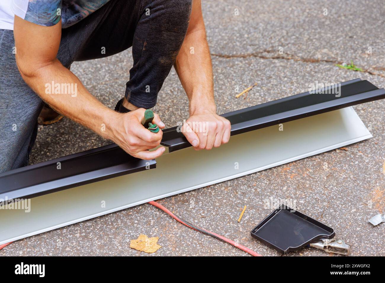 Worker cuts aluminum rain gutters to required size after bending them ...