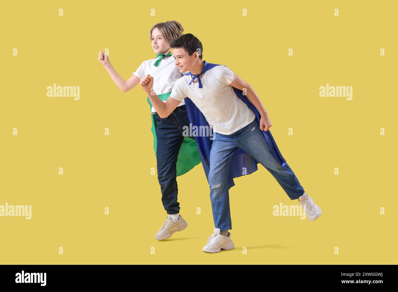 Happy brothers dressed as superheroes jumping on yellow background ...