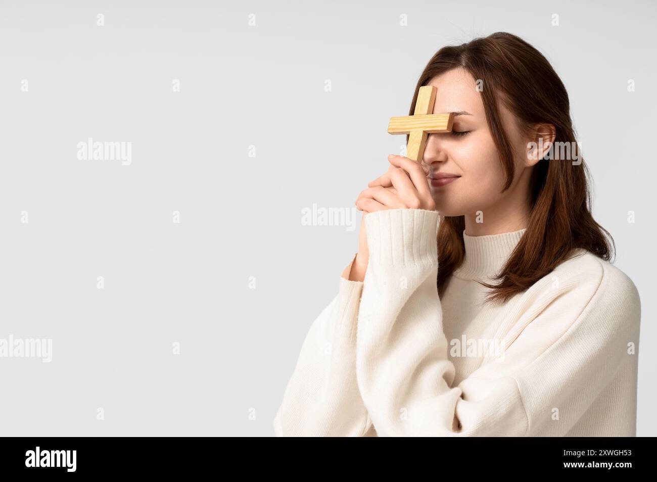 Religious young woman praying with wooden cross on white background ...