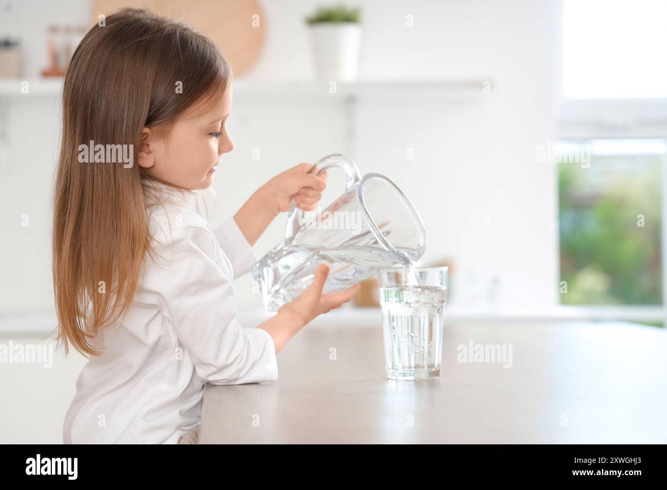 Cute little girl pouring water into glass in kitchen Stock Photo - Alamy