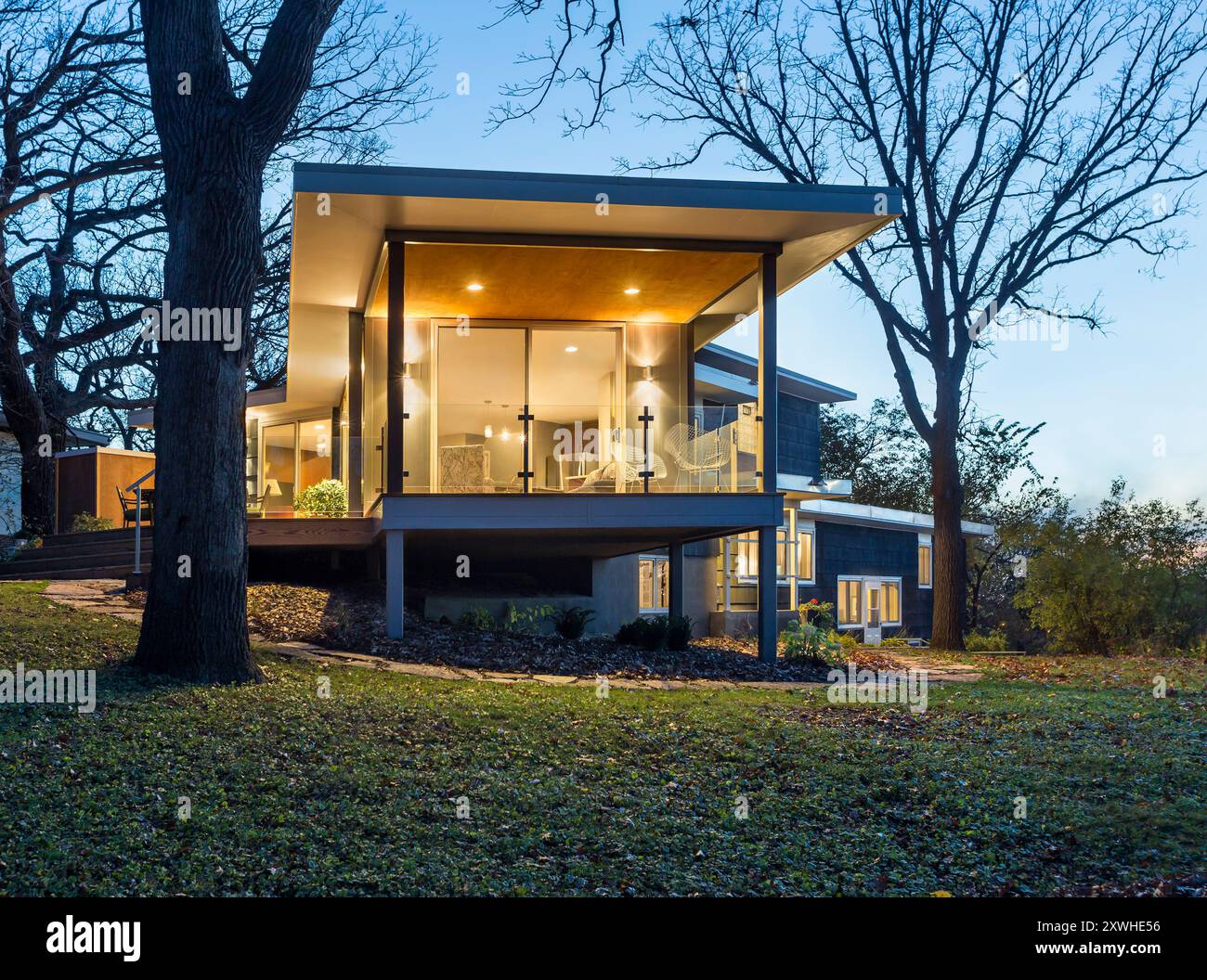 Modern addition to house with raised deck seen with lights on at dusk ...