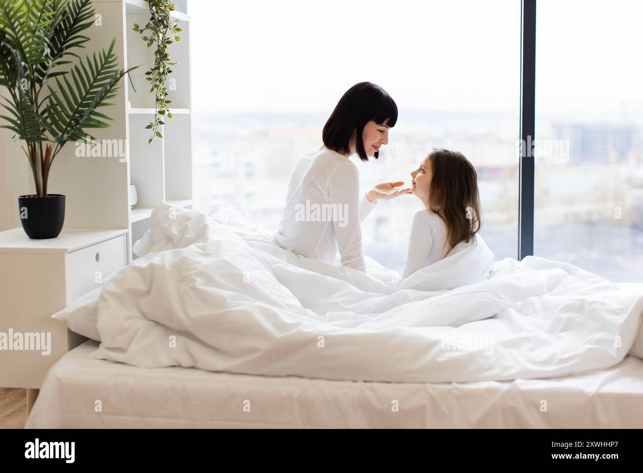 Mother and daughter bonding in bed facing window in morning light Stock Photo - Alamy