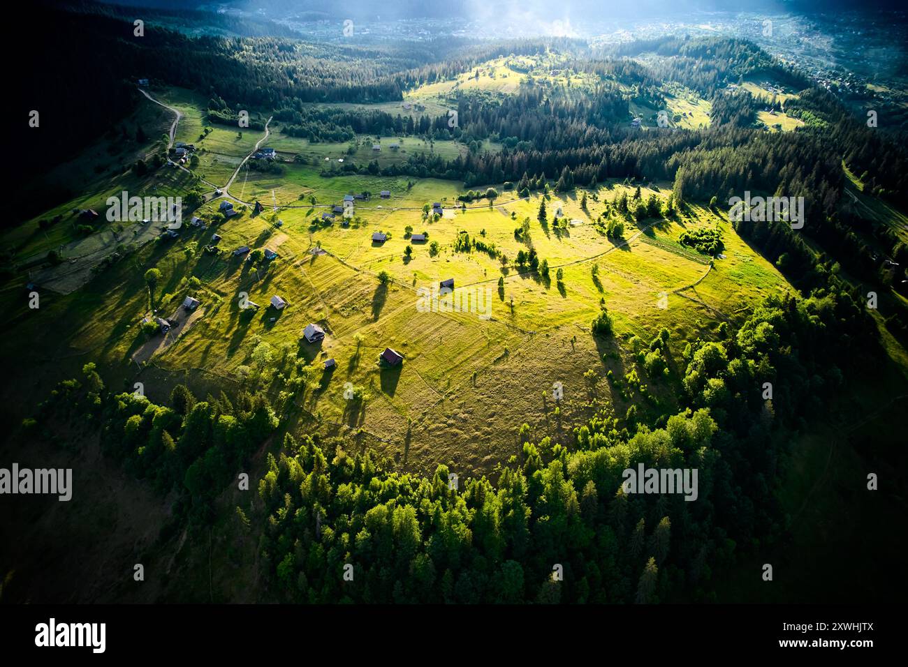 Aerial view of sunlit valley, dotted with small houses and winding ...