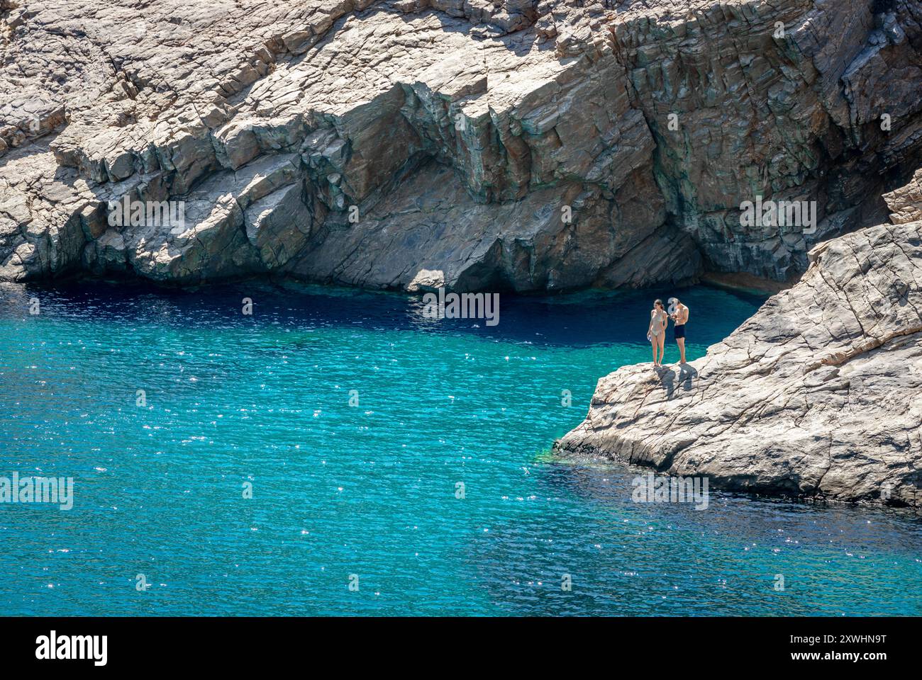 A young couple stands on the cliffs at the far end of Mouros beach, an ...