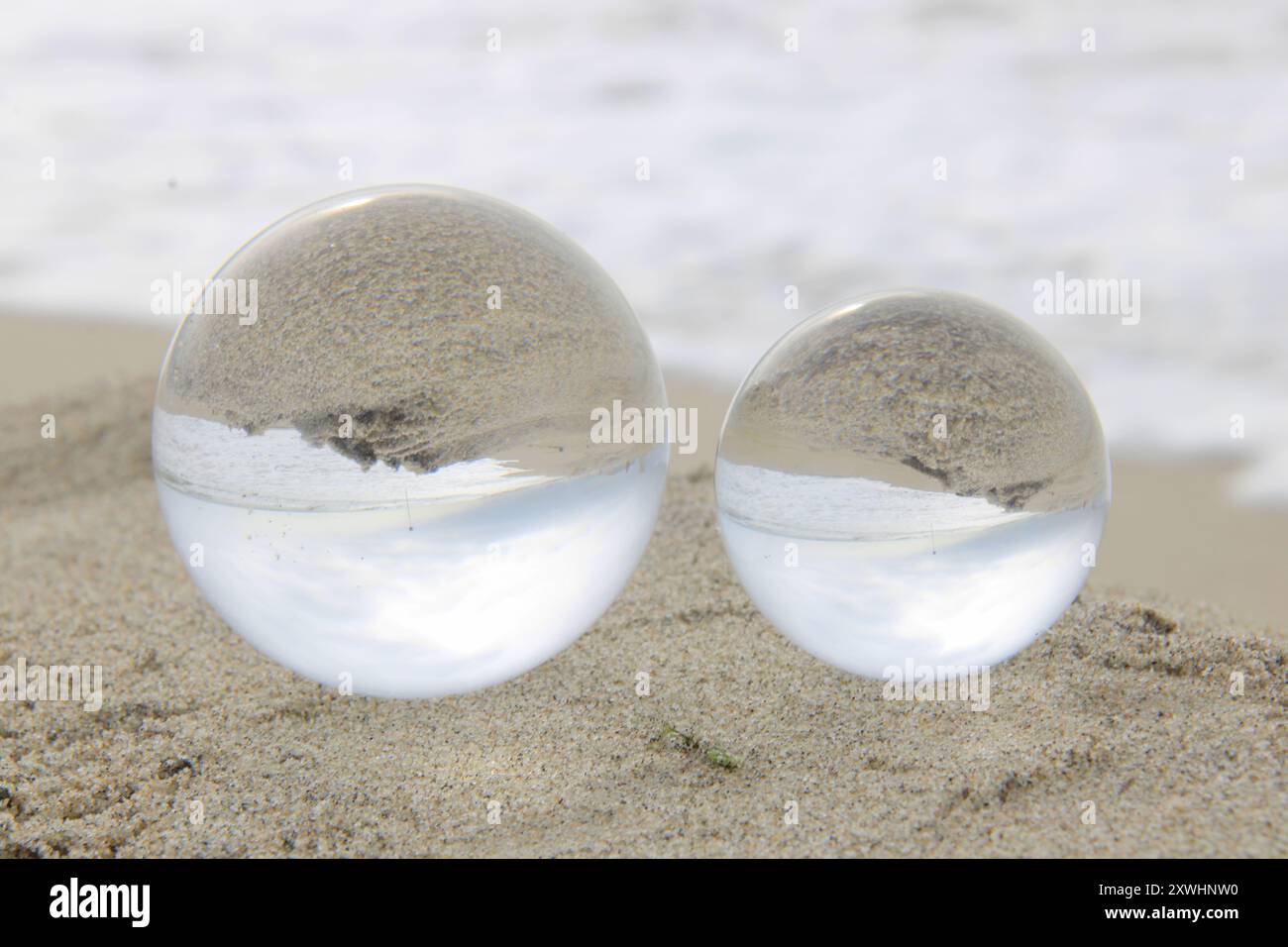 Two crystal balls reflecting a sandy beach and ocean waves, creating a ...
