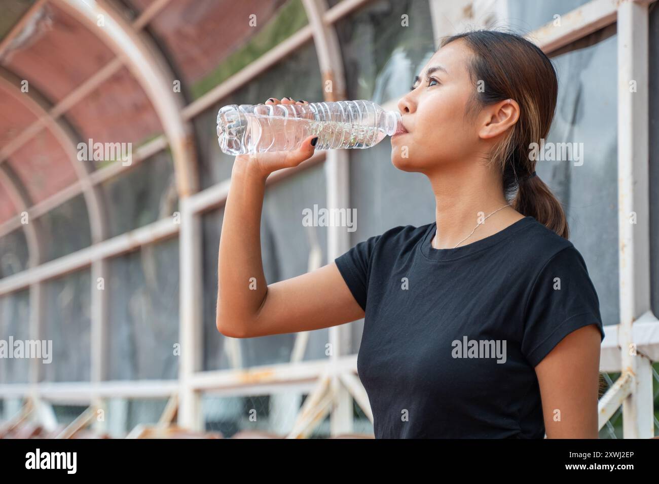 Tired young female runner drinking water from a plastic bottle during ...