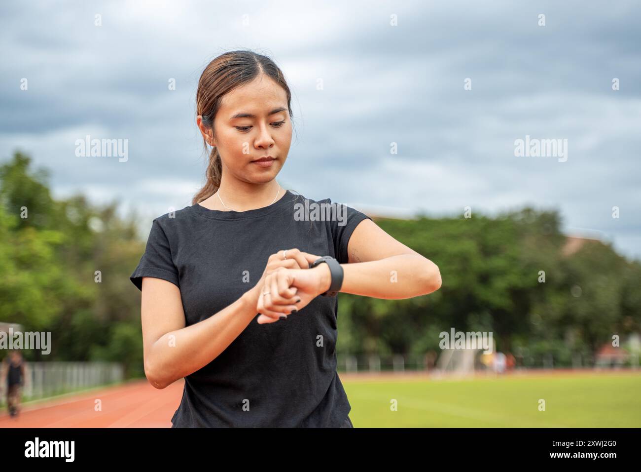 Young Asian female runner checing her run time on her smart watch after ...