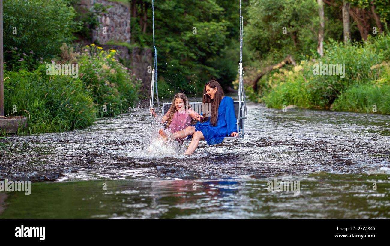 laughing woman and a young girl swing over a fast-flowing river ...