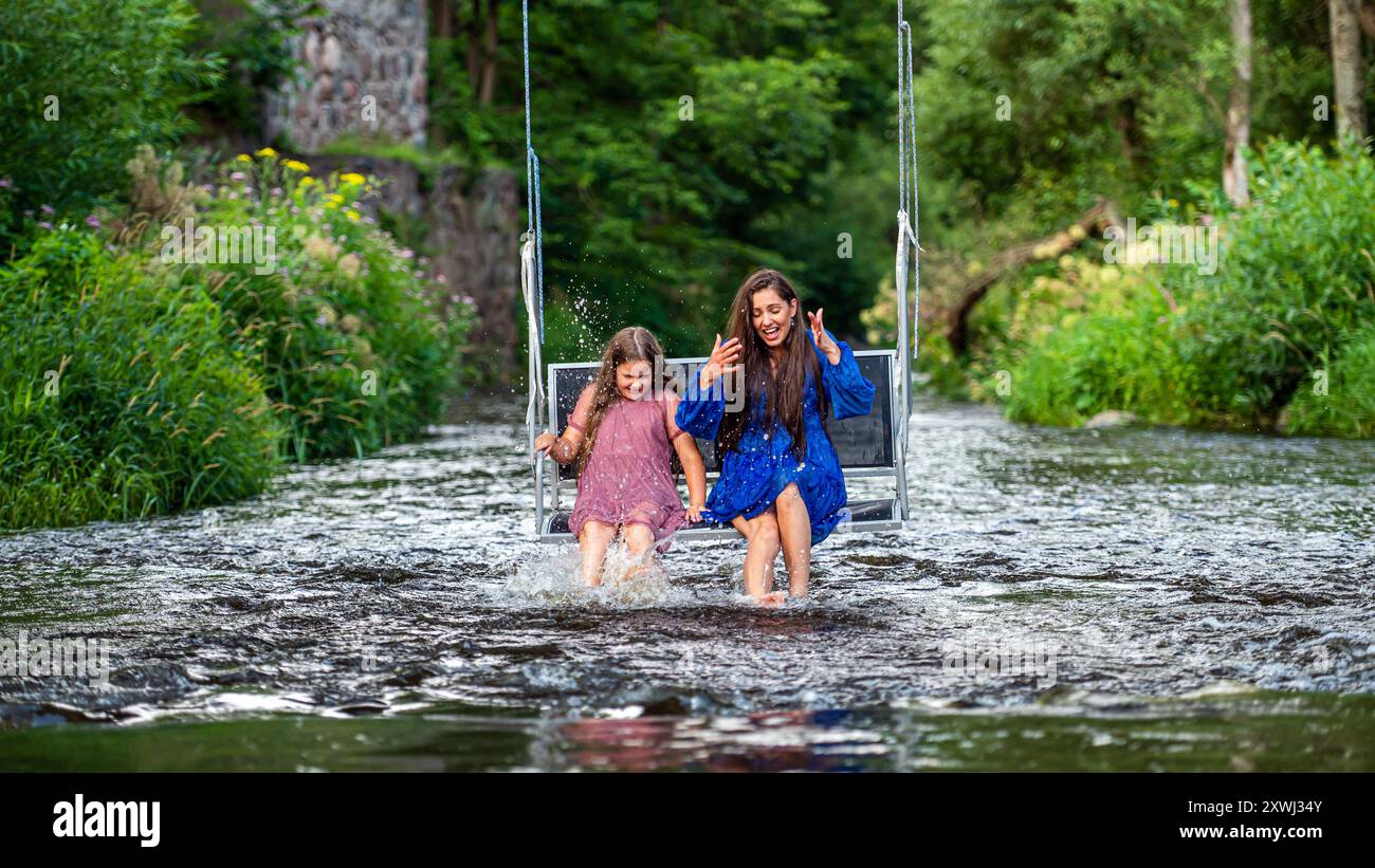 laughing woman and a young girl swing over a fast-flowing river ...