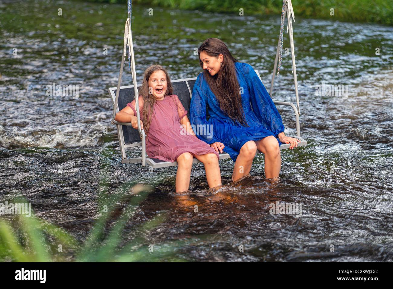 laughing woman and a young girl swing over a fast-flowing river ...