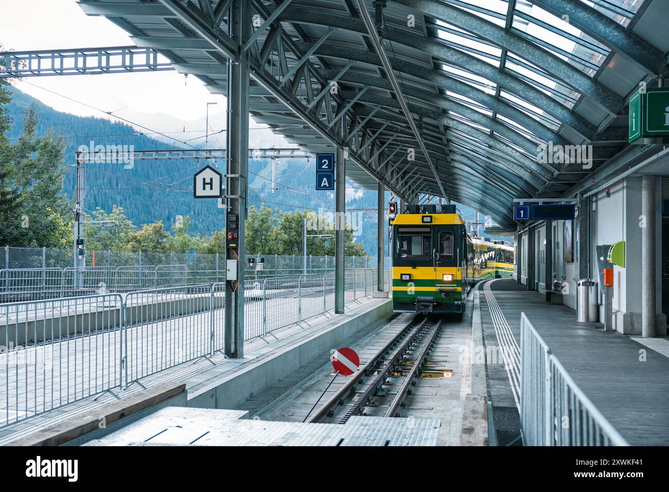The train is coming on railway to stop at station among Swiss Alps in ...