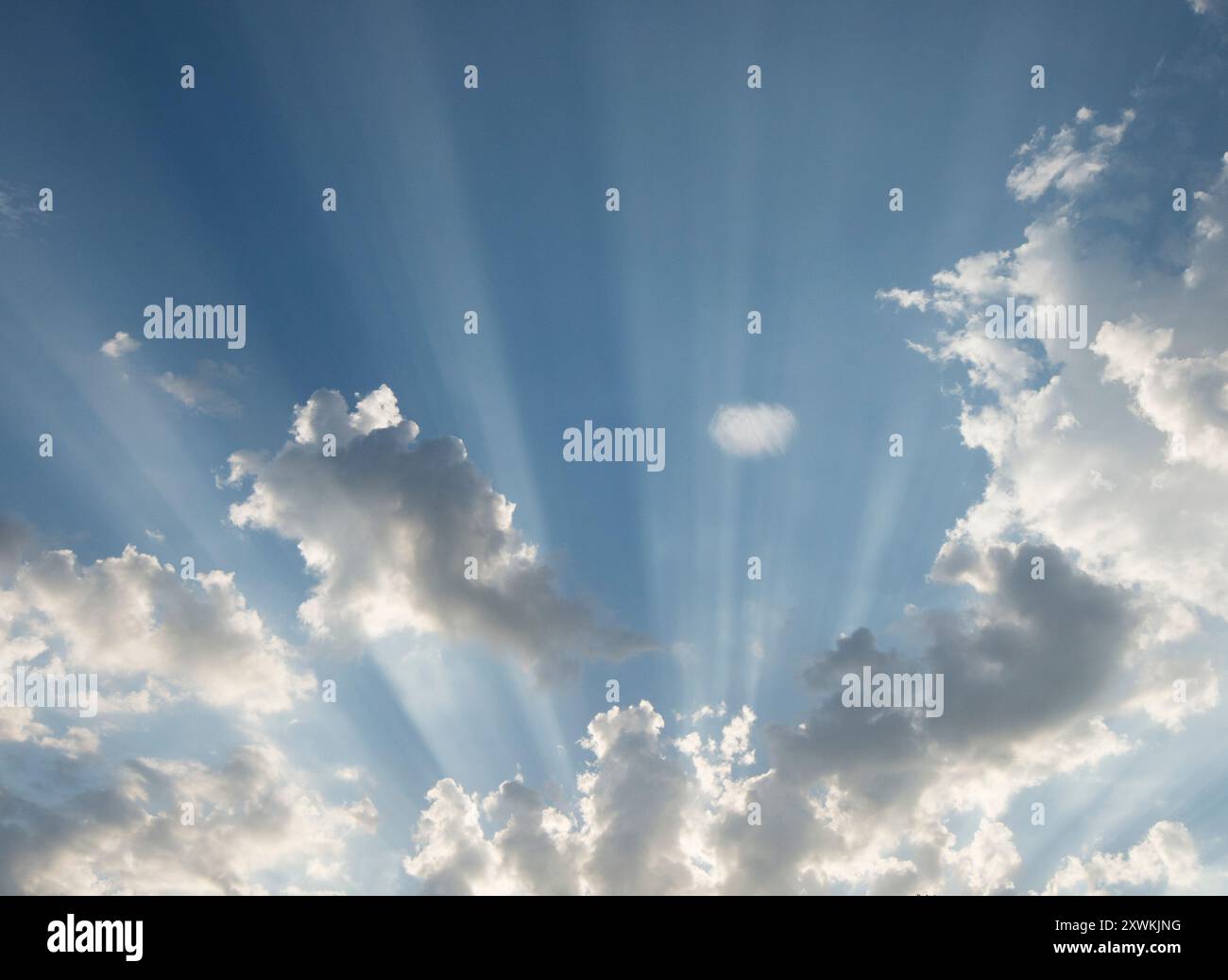 sun rays sweeping across a blue sky from behind clouds lighting up the ...
