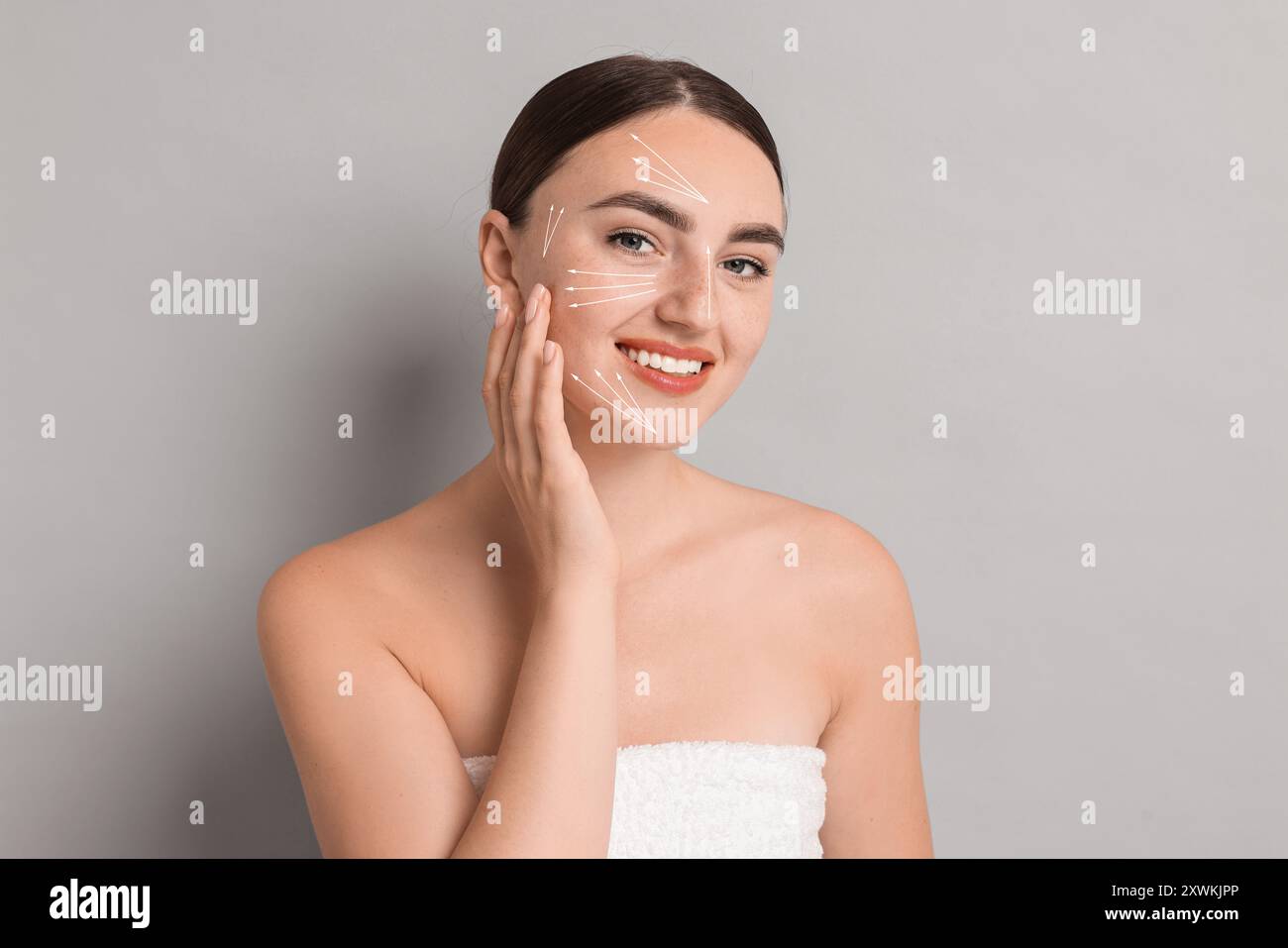 Beautiful young woman doing face massage with fingers on grey ...