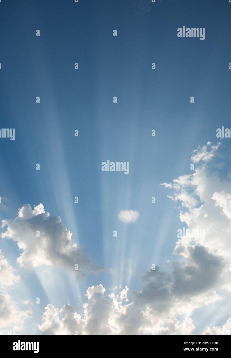 sun rays sweeping across a blue sky from behind clouds lighting up the ...