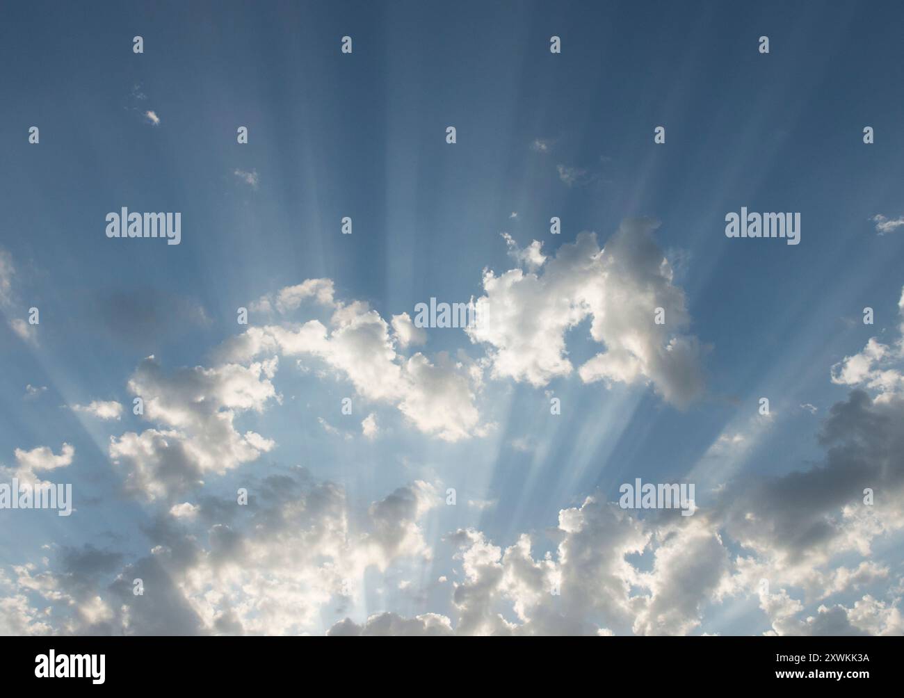 sun rays sweeping across a blue sky from behind clouds lighting up the ...