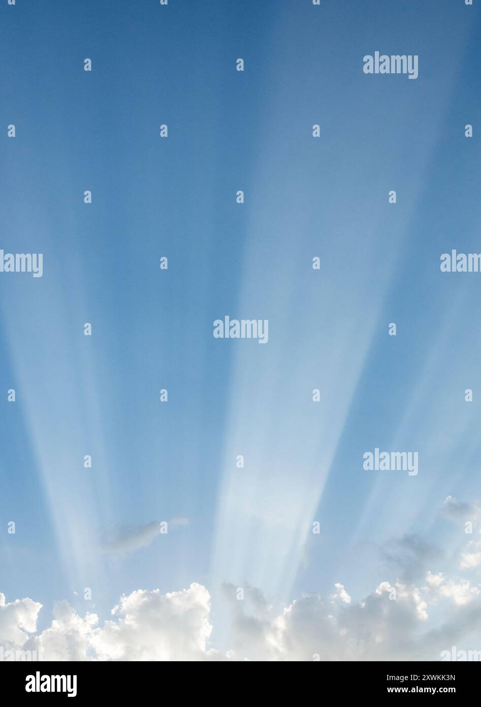 sun rays sweeping across a blue sky from behind clouds lighting up the ...