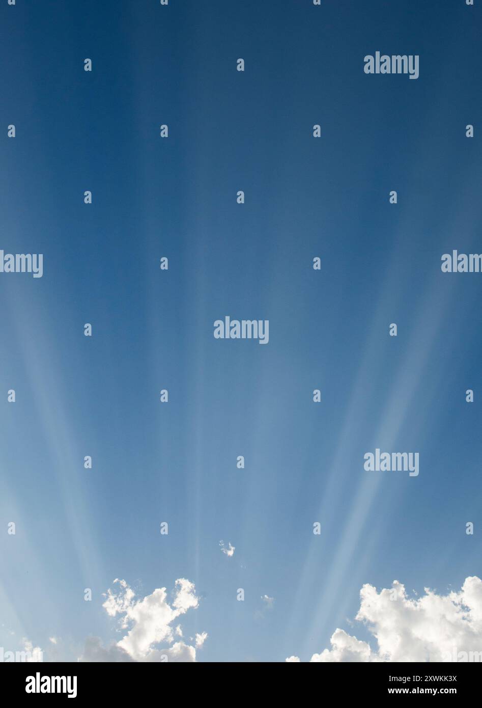 sun rays sweeping across a blue sky from behind clouds lighting up the ...