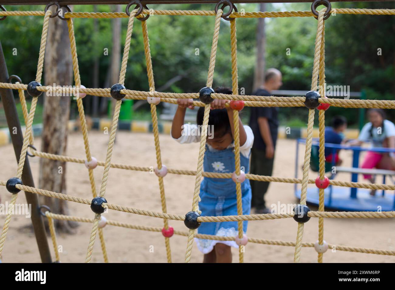 A young girl climbs a rope ladder at a playground, full of energy and ...